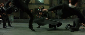 Neo using a weapon to fend off scores of Smith clones